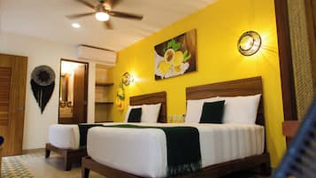Quarto de hotel com duas camas, ventilador de teto, ar condicionado fixado na parede e uma pintura de frutas.