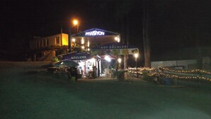 Um mercado noturno ao ar livre com barracas de comida e um letreiro chamativo com a palavra 'PANSIYON'.