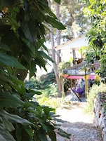 Uma área de estar coberta ao ar livre, com mesas e cadeiras, rodeada por árvores e vegetação.