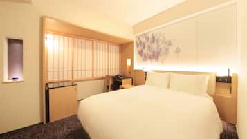 Quarto de hotel com uma cama grande, uma mesa e uma cadeira. Há uma televisão na parede e um quadro sobre a cama.