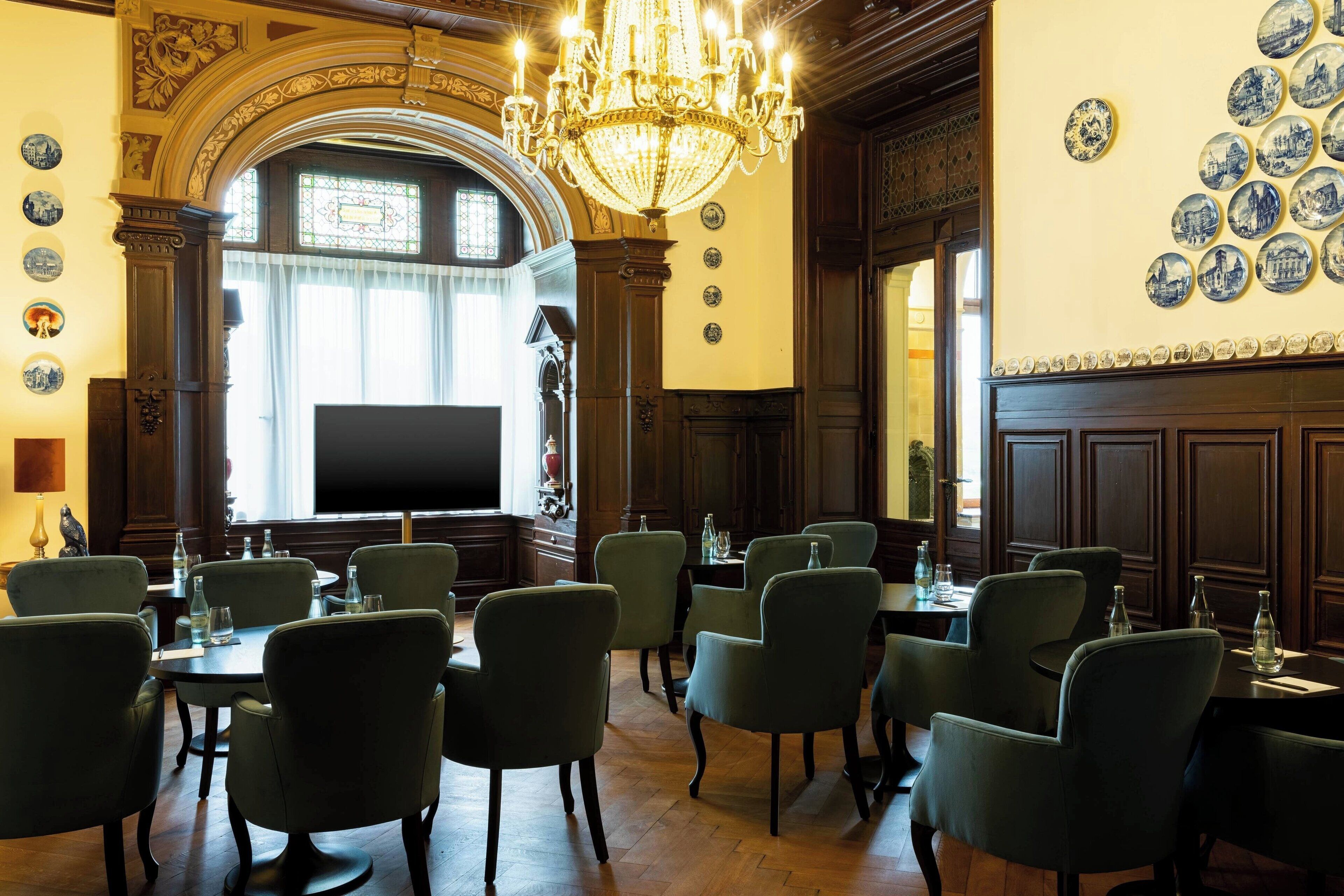 Uma sala de jantar com várias mesas e cadeiras, um candelabro e uma janela grande com vista.