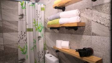 Casa de banho com sanita, cortina de chuveiro e prateleiras com toalhas e artigos de higiene pessoal.