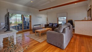 Uma sala de estar ampla com piso de madeira, um sofá cinza, uma mesa de centro de madeira e uma televisão em um suporte branco.