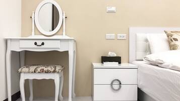 Quarto com uma cama branca, uma mesinha de cabeceira com um estojo de lenços, cômoda branca com espelho e uma poltrona floral, e parede bege.