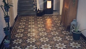 Um corredor com piso estampado, escada, fogão a lenha e plantas em vasos.