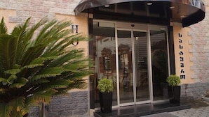 Entrada de hotel com fachada de pedra, portas de vidro e toldo preto.