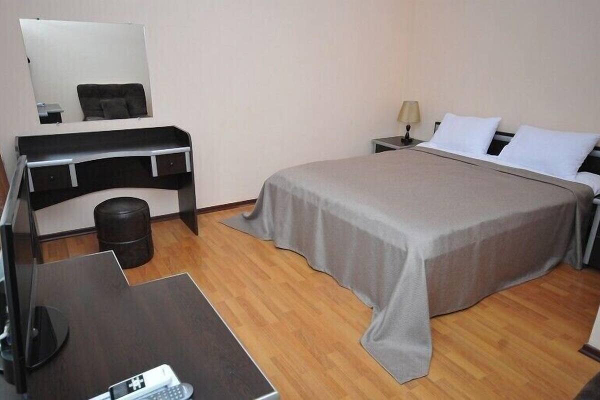 Quarto de hotel com cama, escrivaninha, cadeira, abajur e espelho.