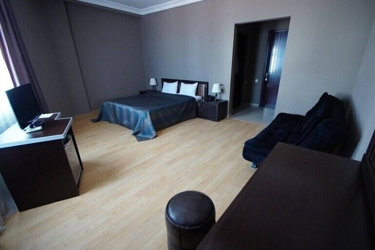 Quarto de hotel com uma cama, mesas de cabeceira, uma escrivaninha com computador e uma cadeira.
