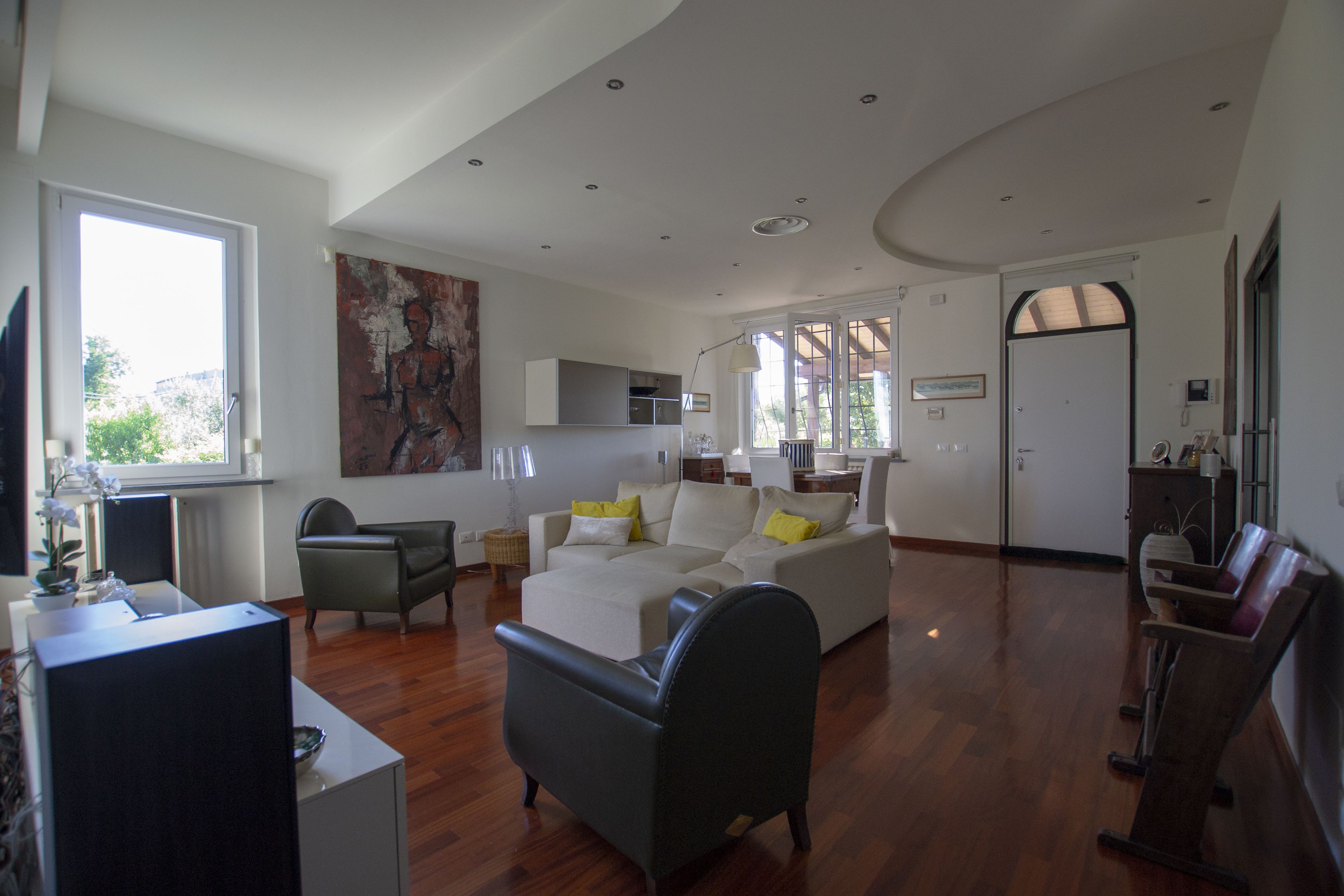 Uma sala de estar espaçosa com um sofá grande, uma mesa de centro e uma televisão. Há uma porta que dá para outro cômodo e uma janela que proporciona iluminação natural.