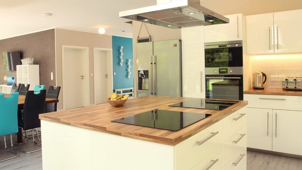 Cozinha moderna com ilha central, eletrodomésticos de aço inoxidável e área de refeições com cadeiras e mesa.