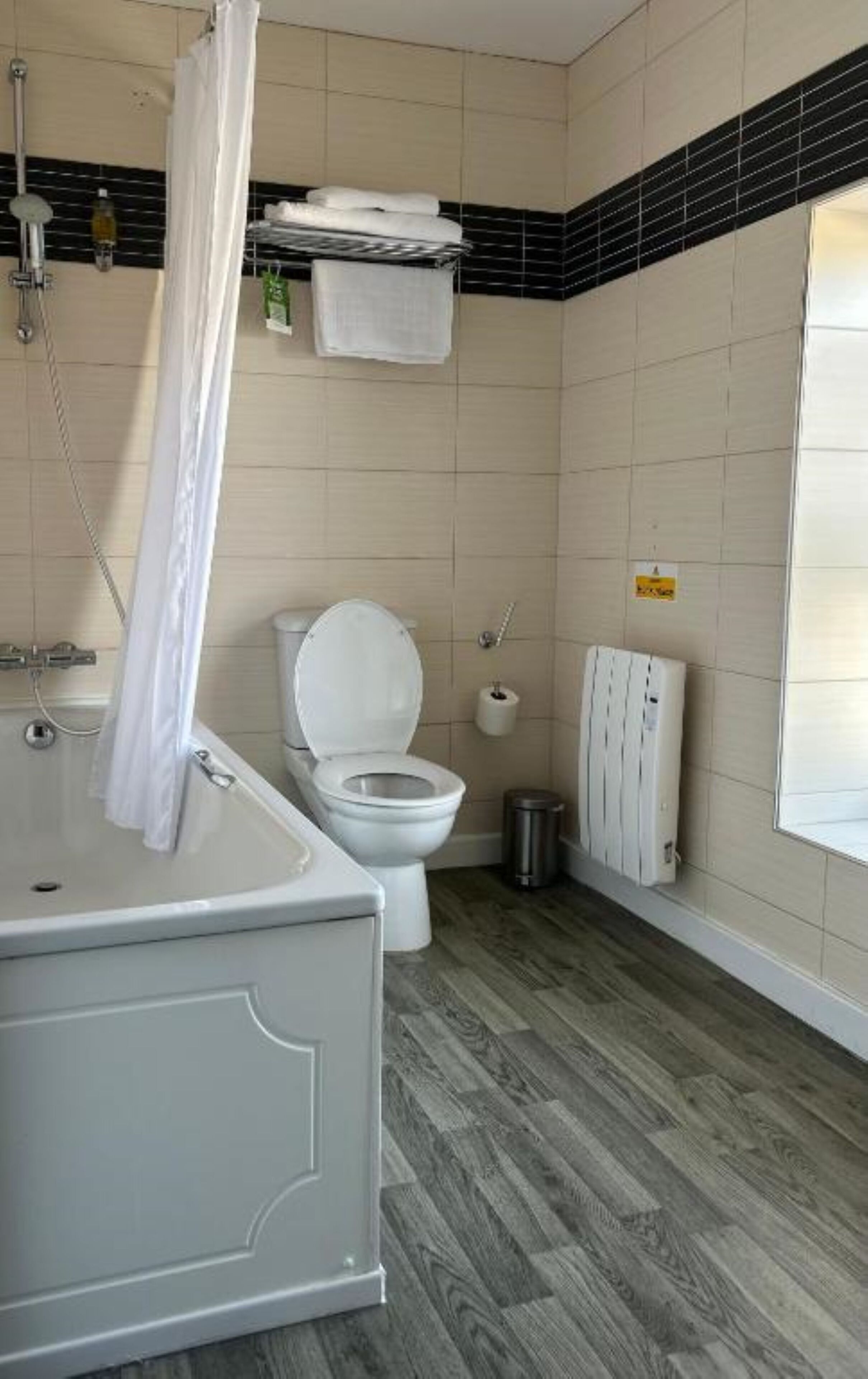 Casa de banho com banheira, sanita e chuveiro. Há um porta-toalhas sobre a sanita e um rolo de papel higiénico na parede.