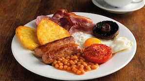 Prato de comida de café da manhã com ovos, salsichas, bacon, torradas, feijão e um tomate.