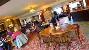 Um restaurante com mesas e cadeiras de madeira, paredes de pedra e luminárias pendentes.