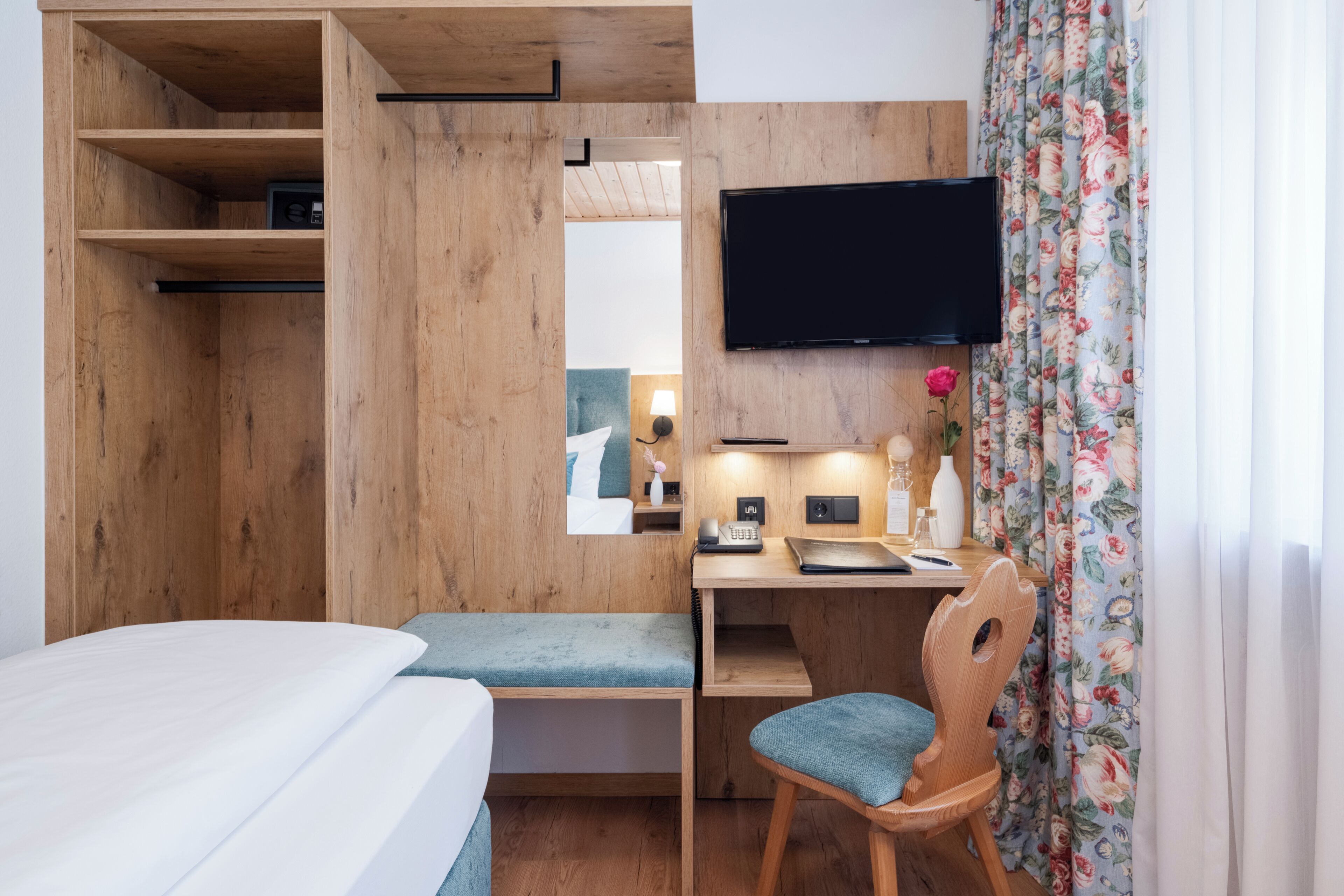 Um quarto com uma cama, uma escrivaninha com cadeira, uma televisão e um espelho.
