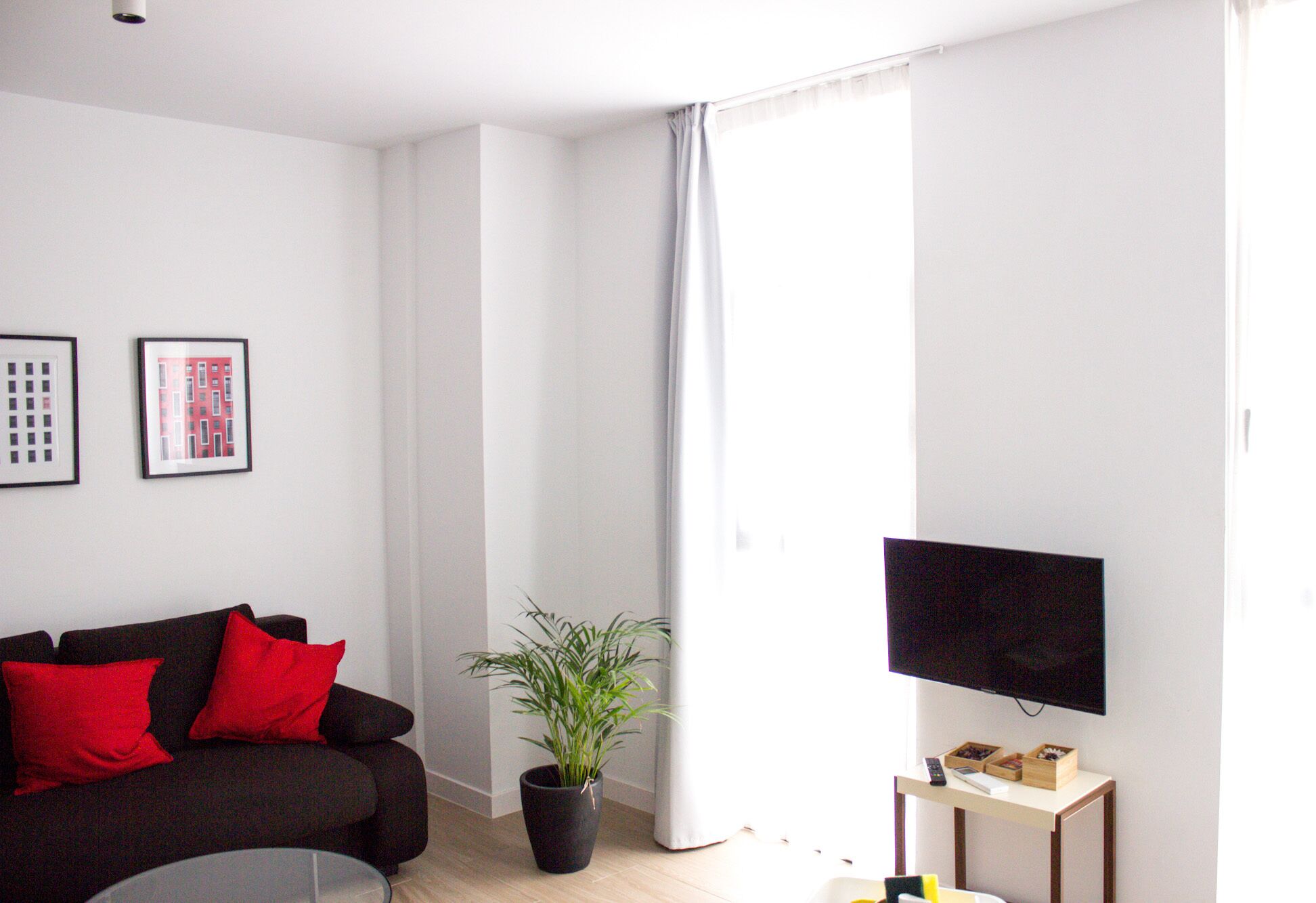 Uma sala de estar moderna com um sofá preto, almofadas vermelhas, uma planta em vaso, uma TV de tela plana e quadros na parede.
