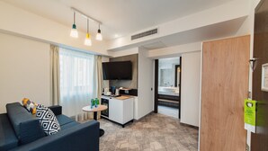 Quarto de hotel moderno com sofá, pequena cozinha, televisão e banheiro.