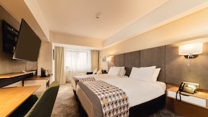 Quarto de hotel com uma cama grande, uma escrivaninha, uma cadeira, uma TV e um telefone na mesa de cabeceira.