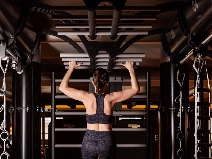 Uma academia com equipamentos de ginástica e uma pessoa fazendo barra fixa.