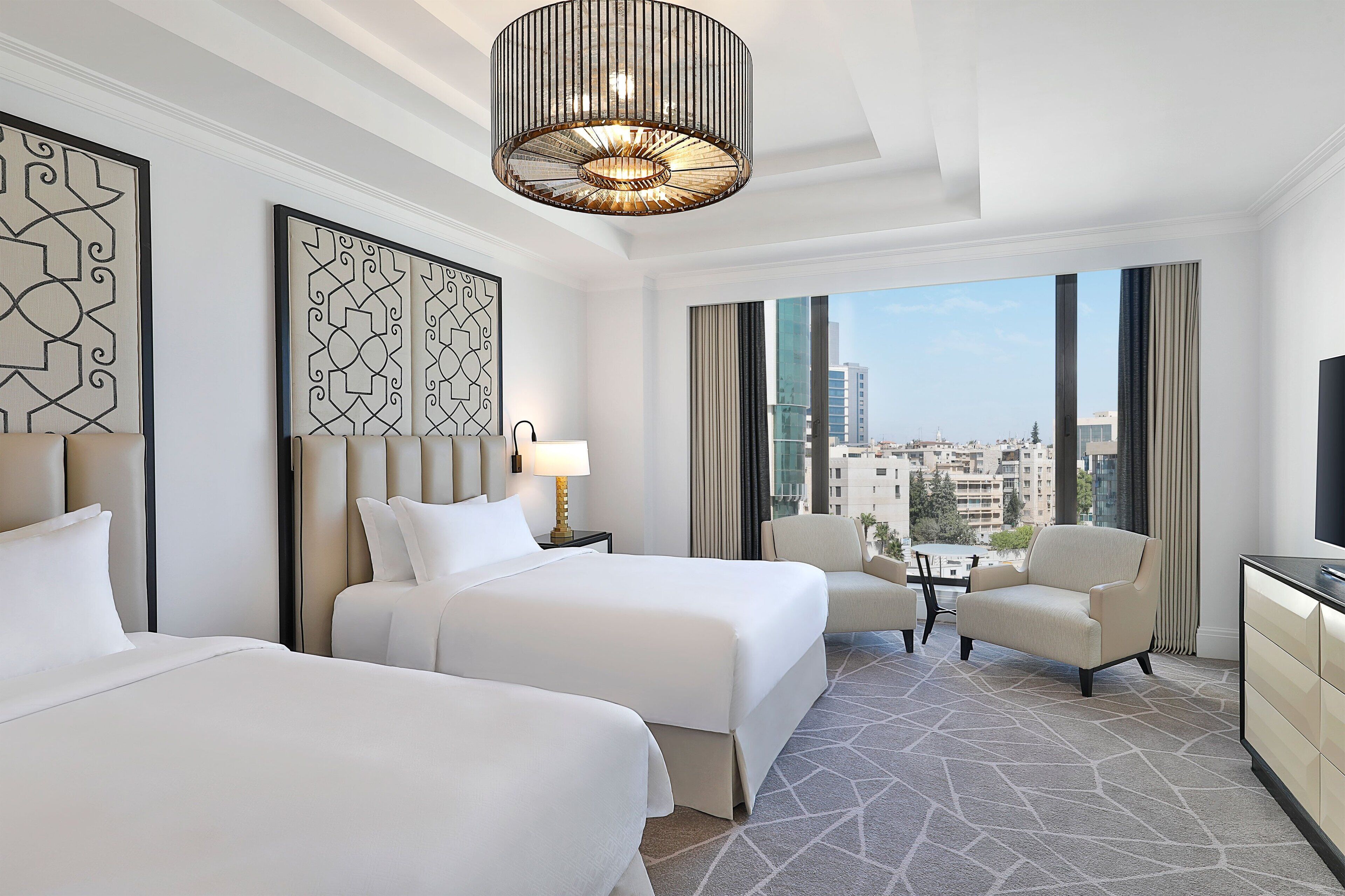 Quarto de hotel com duas camas, um espaço de estar, televisão e vista para a cidade.