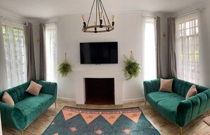 Uma sala de estar com dois sofás verdes, uma lareira, uma televisão de tela plana e um tapete estampado.