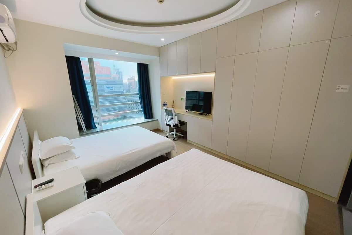 Quarto de hotel com duas camas, televisão, secretária e janela com vista para a cidade.