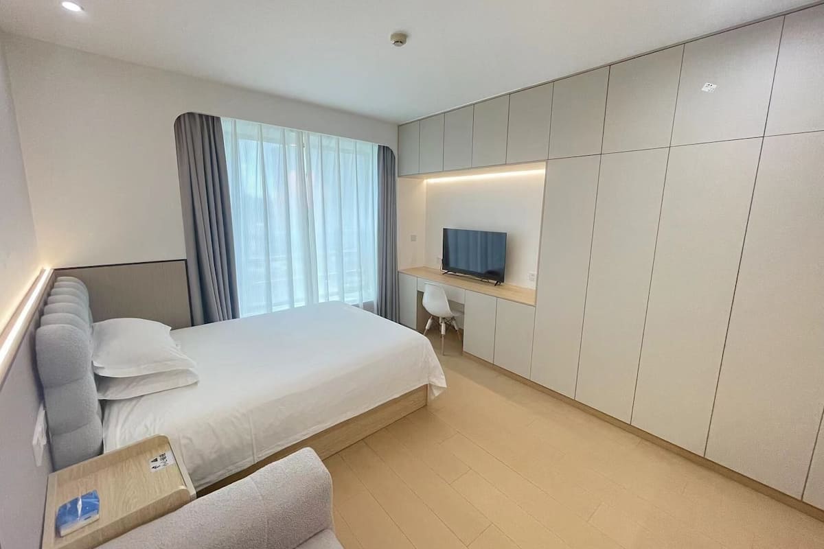Quarto de hotel moderno com uma cama grande, uma mesa com cadeira, uma televisão e um guarda-roupa.