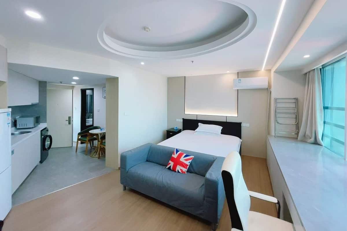 Quarto de hotel moderno com cama, sofá, pequena cozinha e banheiro.