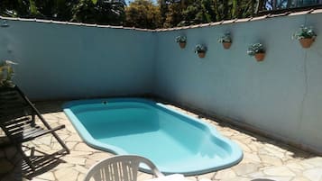 Pequena piscina ao ar livre com piso de pedra, cercada por um muro baixo.