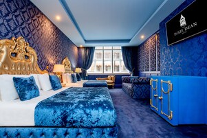 Quarto de hotel luxuoso com uma cama grande, um sofá azul estofado e um armário azul.