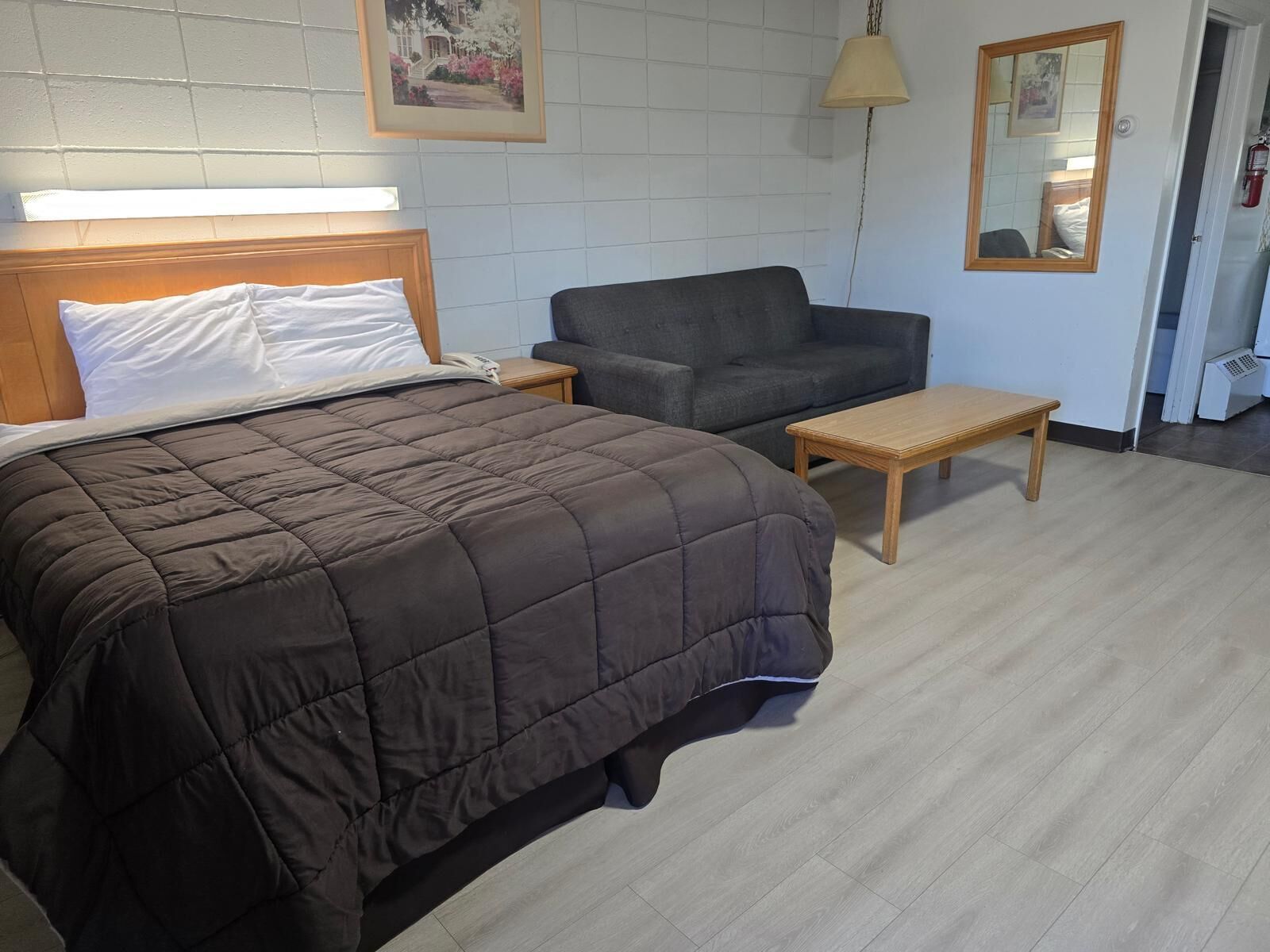 Quarto de hotel com uma cama grande, um sofá cinzento, uma mesa de centro de madeira e um pequeno banco.