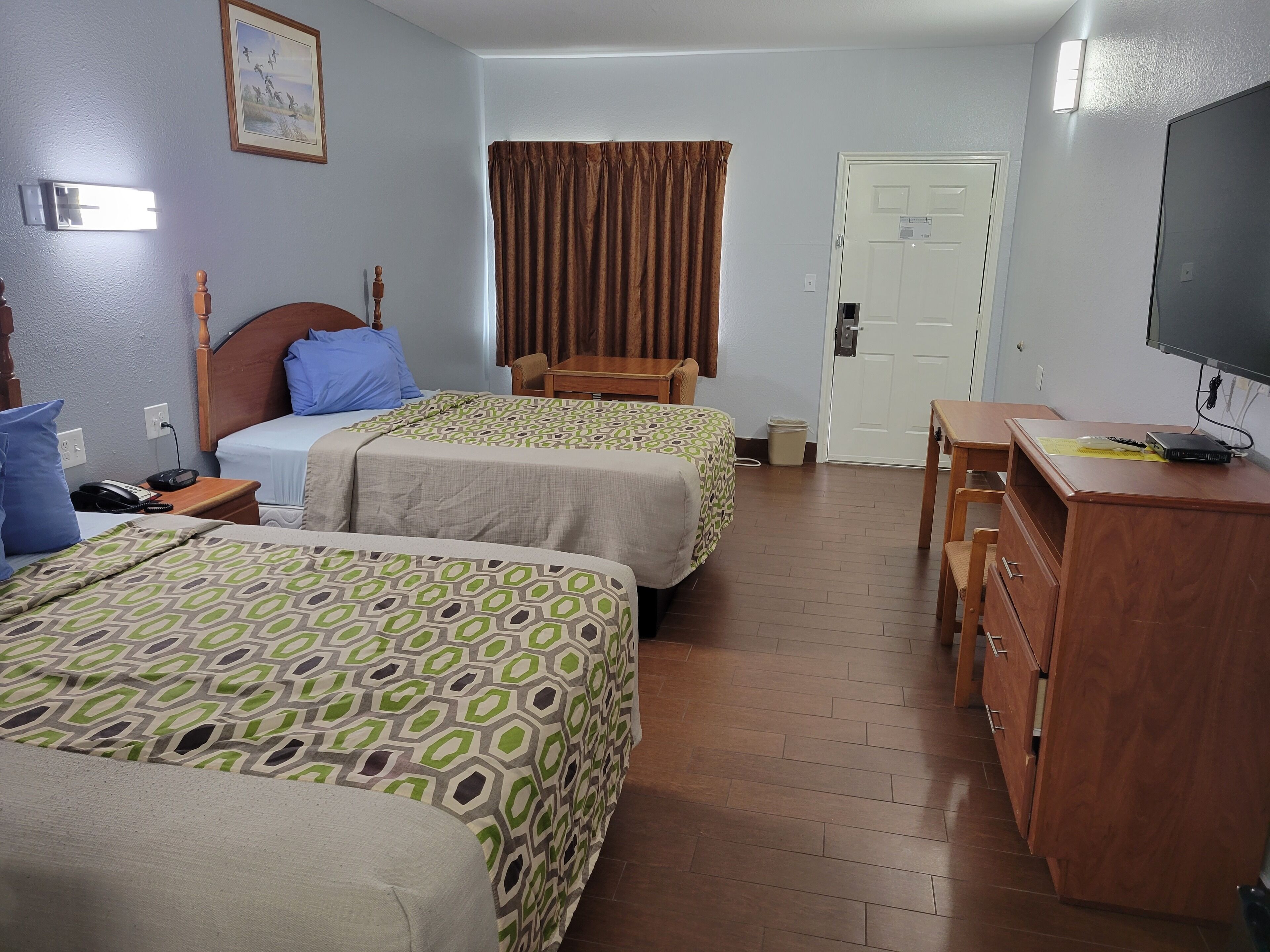 Quarto de hotel com duas camas, uma escrivaninha, uma cadeira, uma televisão e uma porta.
