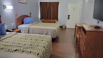 Quarto de hotel com duas camas, uma escrivaninha, uma cadeira, uma televisão e uma porta.