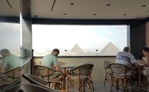 Um restaurante com vista para as pirâmides, cadeiras de vime e uma mesa de vidro.