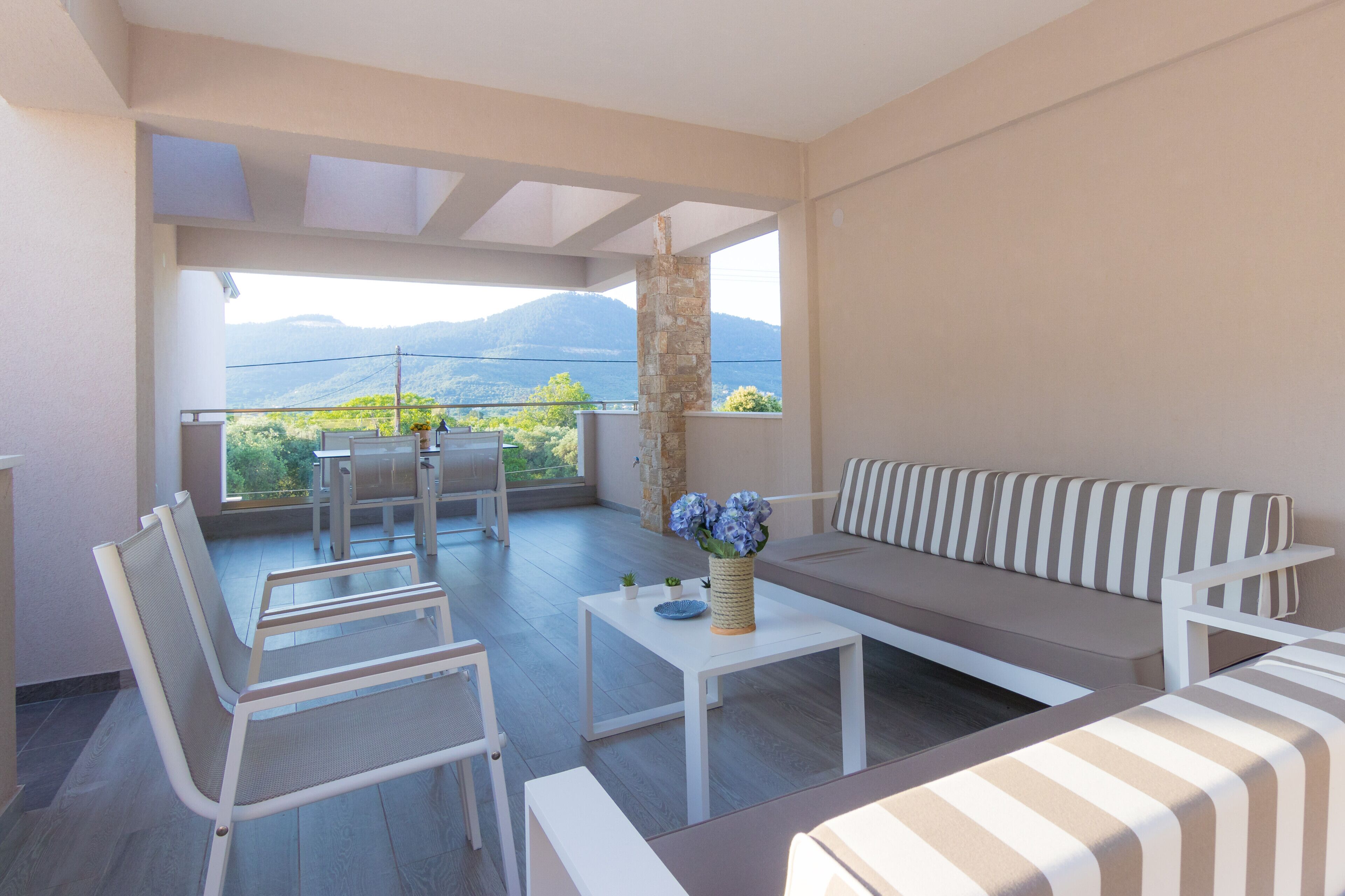 Uma sala de estar moderna com sofá, cadeiras e mesa de centro. Uma varanda com vista para as montanhas é visível pela janela.