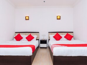 Quarto de hotel com duas camas, cada uma com colcha vermelha e branca, e duas luminárias fixadas na parede.