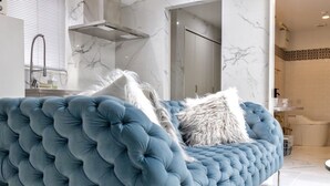 Uma sala de estar moderna com um sofá azul estofado, um cobertor branco fofo e uma parede com padrão de mármore.