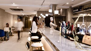 Uma área de bar moderna com um balcão comprido, banquetas e diversos frascos e copos.