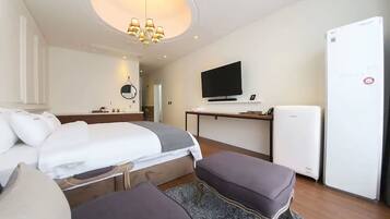 Quarto de hotel com uma cama, uma escrivaninha, uma televisão e um frigorífico.