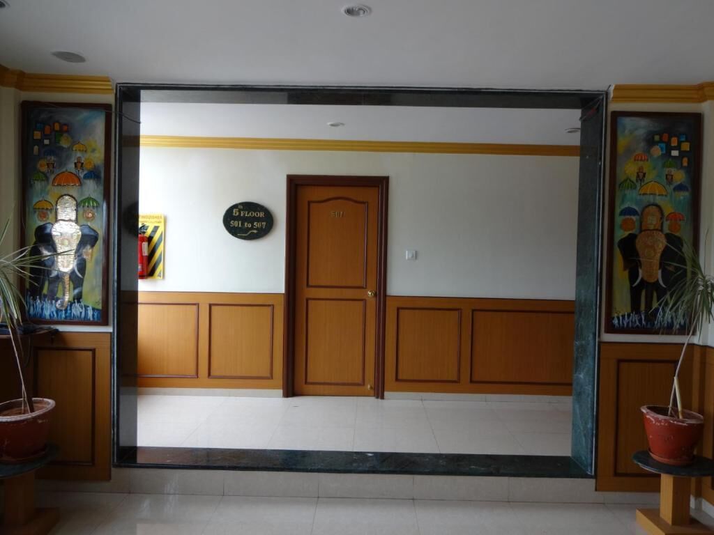 Um saguão de hotel com porta de madeira, placa indicando o sexto andar e plantas em vasos.