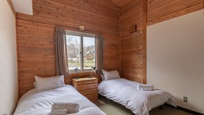 Quarto com painéis de madeira, duas camas, uma mesa de cabeceira e uma janela com cortinas.