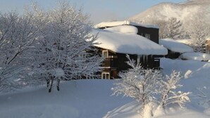 Um edifício coberto de neve com fachada escura, rodeado por árvores e uma montanha ao fundo.