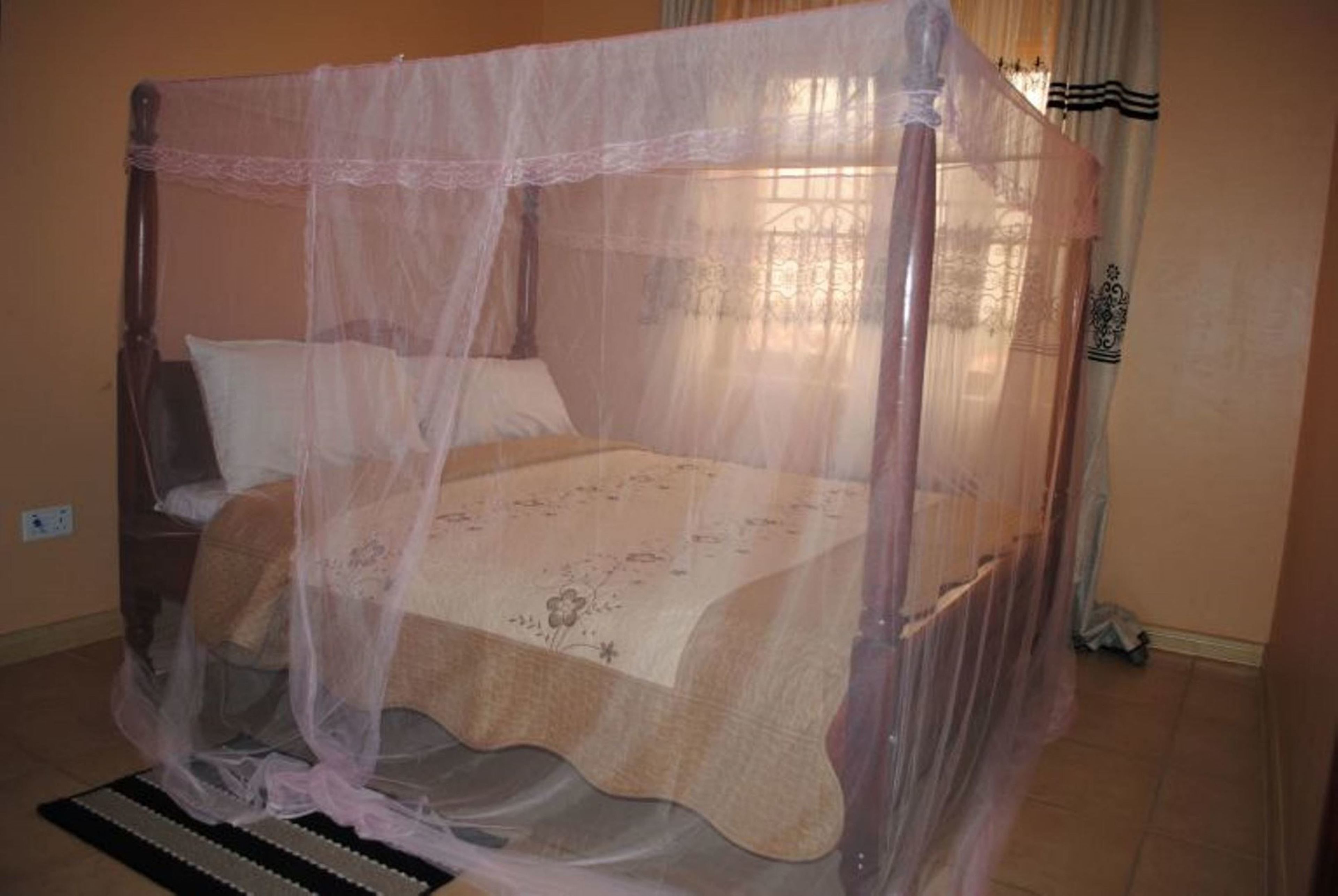 Uma cama de dossel com cortina, uma colcha florida e um tapete listrado.