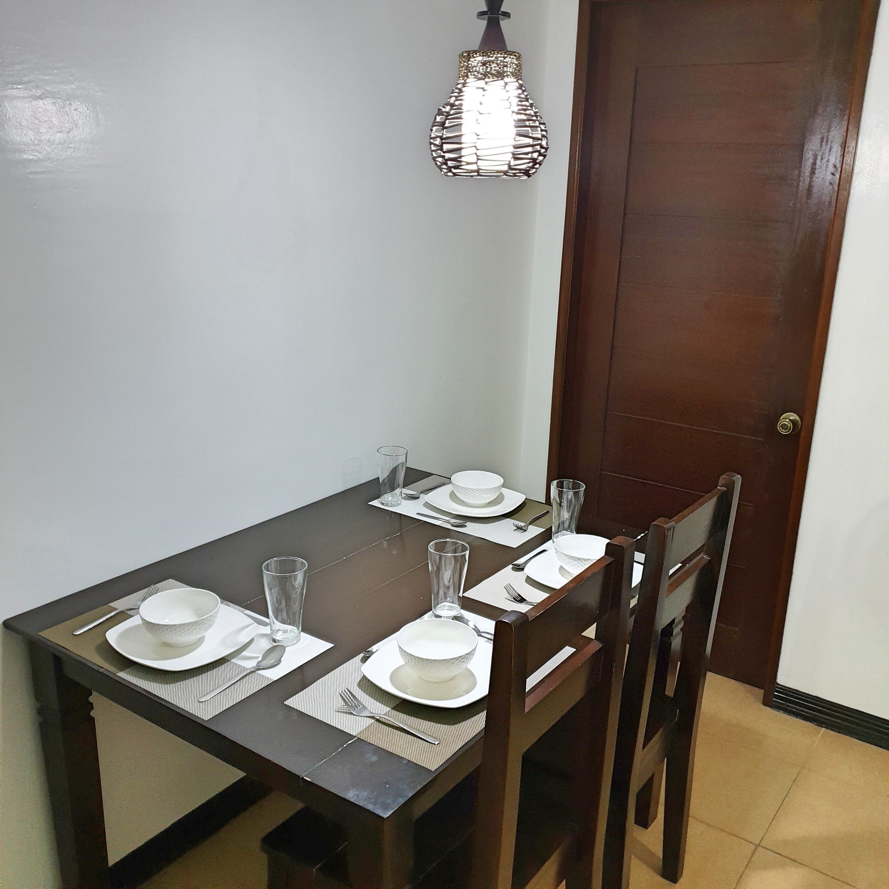 Uma mesa de jantar posta com pratos, tigelas, copos e talheres, com um lustre pendurado acima.