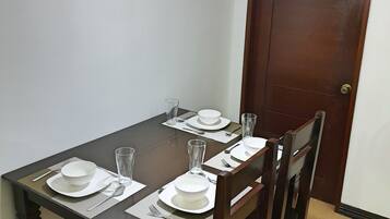 Uma mesa de jantar posta com pratos, tigelas, copos e talheres, com um lustre pendurado acima.