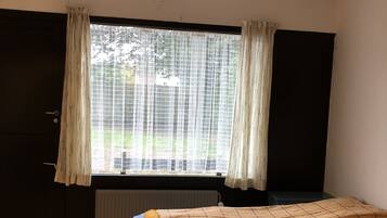 Quarto com duas camas, janela com cortinas, radiador e porta.