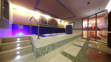 Uma área de spa com piso de ladrilho de pedra, um elemento aquático iluminado em azul e um espaço de estar com vista para o salão de spa.