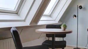 Um quarto com um claraboia, uma mesa redonda com uma planta, uma cadeira preta e um abajur.