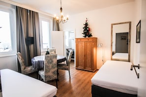 Quarto de hotel com duas camas, uma mesa de jantar com cadeiras em padrão de zebra, um armário de madeira, um pequeno pinheiro de Natal e um espelho na parede.