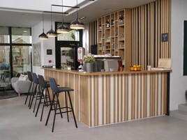 Uma área de bar moderna com balcão de madeira, banquetas e um dispensador de bebidas.