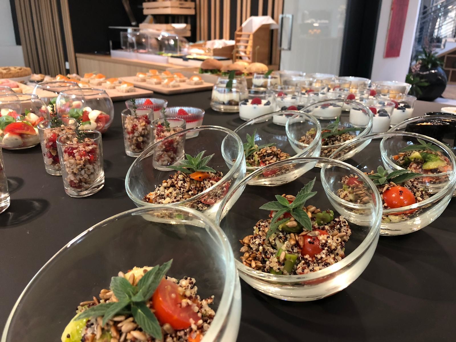 Uma mesa de buffet com diversos pratos, incluindo saladas e sobremesas, servidos em tigelas e pratos de vidro.